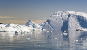 Sunlit iceberg and ice floe in icy waters under a grey sky Royalty-Free ...