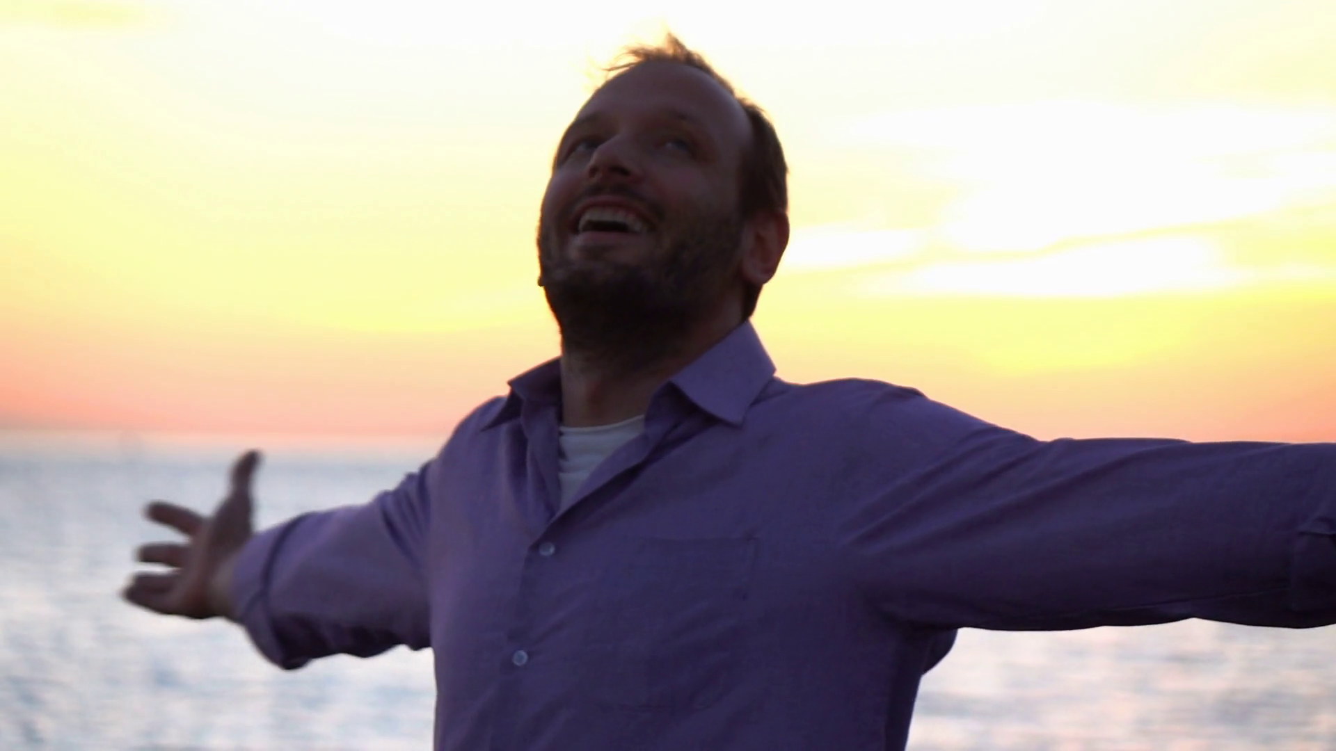 Young, happy man turning around on beach during suset, slow motion ...