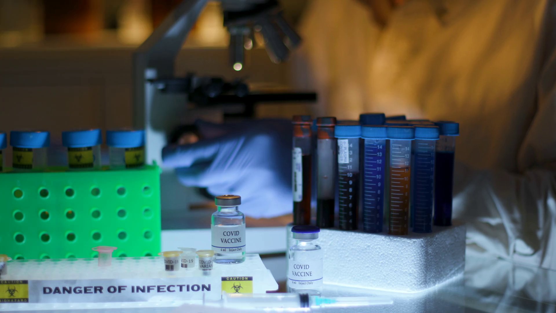 laboratory tech using a microscope with Covid vaccine vial in ...