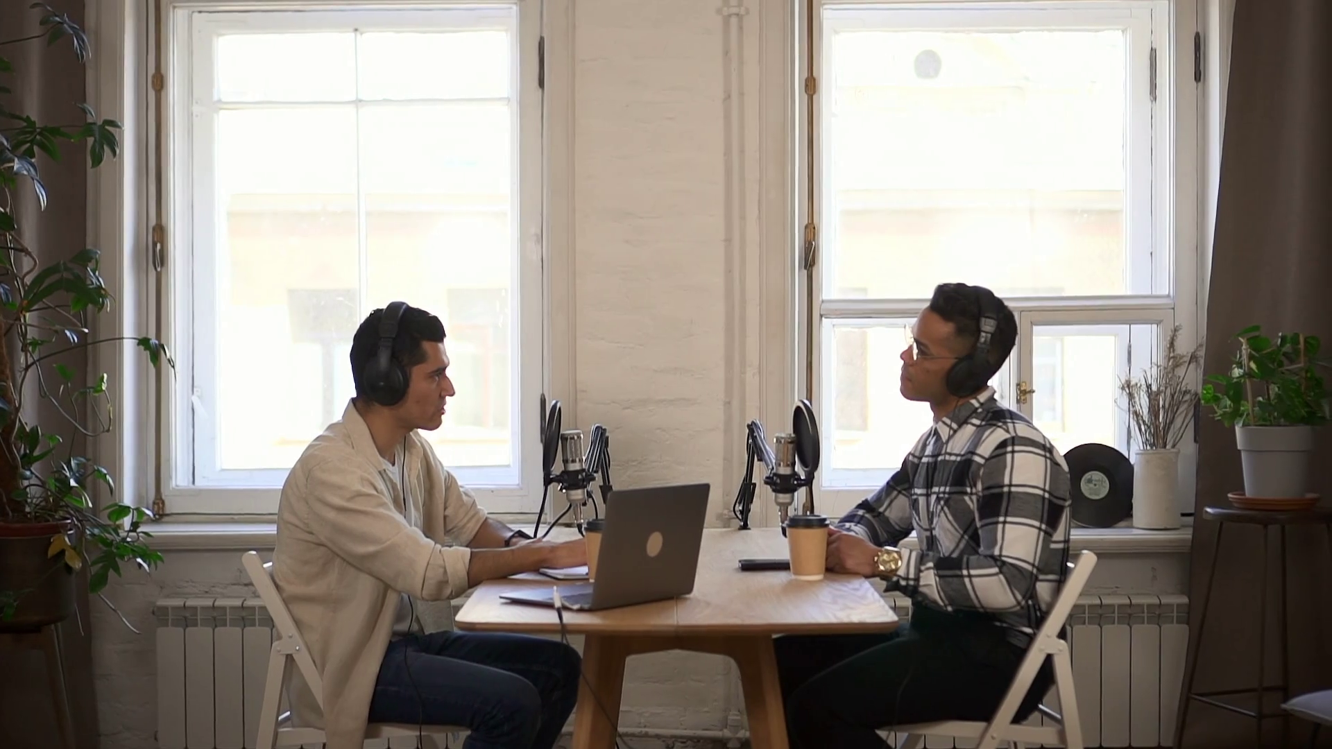 Two male speakers talking and recording podcast at table with laptop in ...