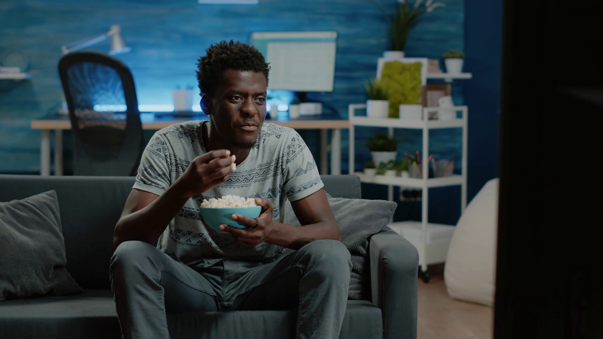 African american man enjoying comedy on television while eating popcorn at home. Black person ...