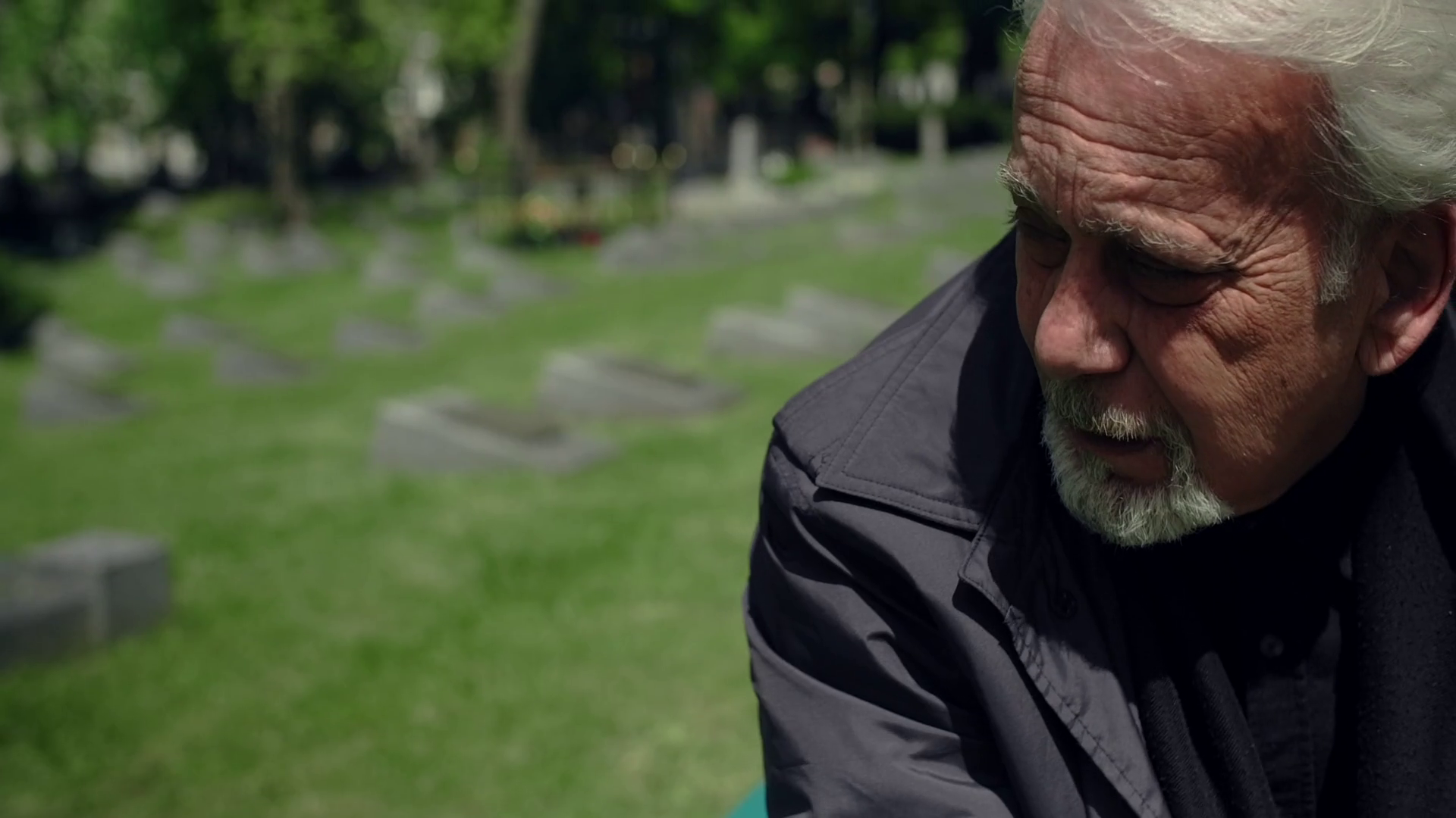 Sad old gray haired man sits on the grave at the cemetery, sorrow and ...