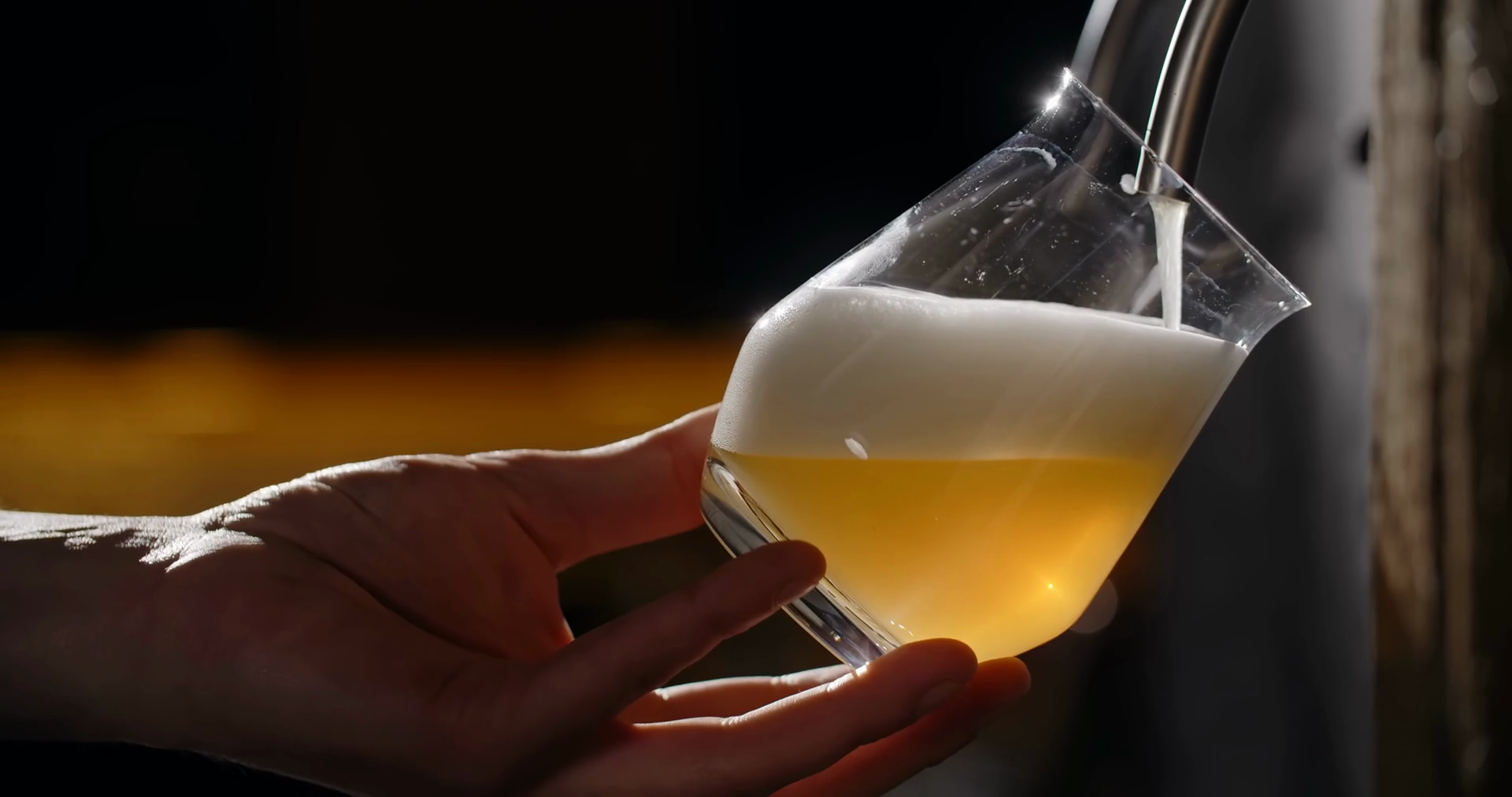 Barman pours unfiltered light beer from the beer tap to the glass in ...