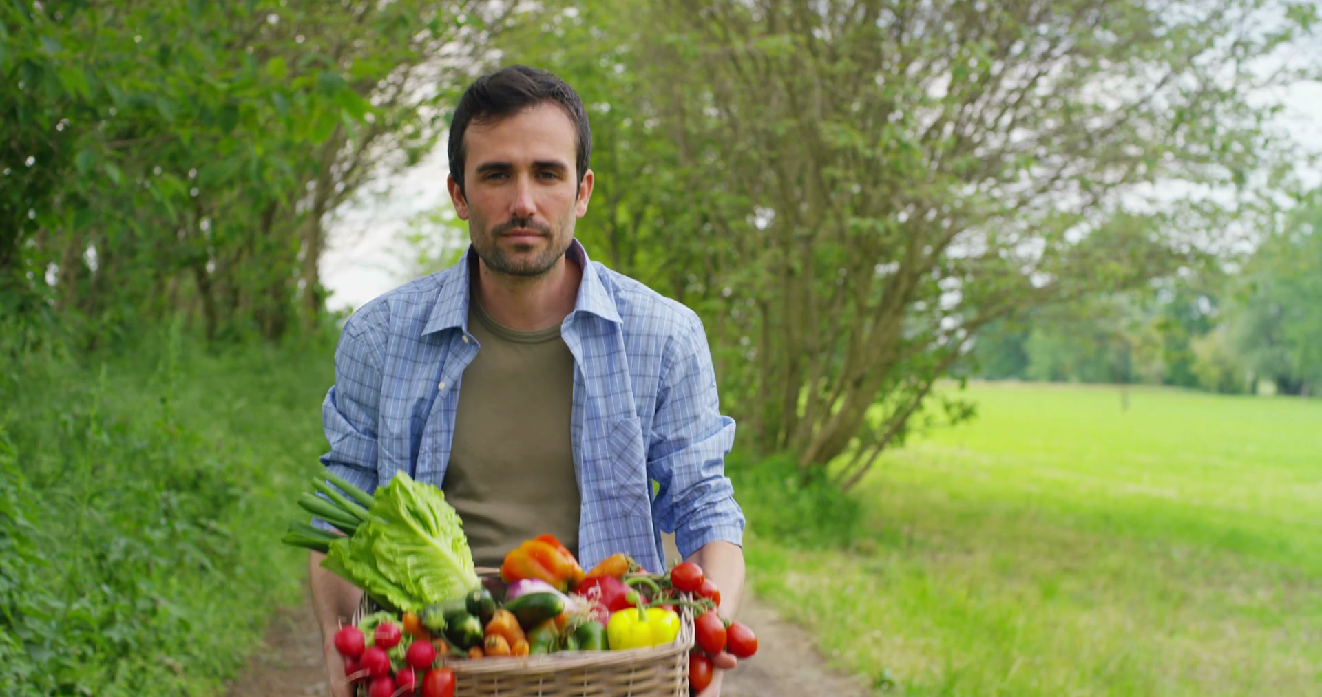 Portrait of a happy young farmer holding fresh vegetables in a basket ...