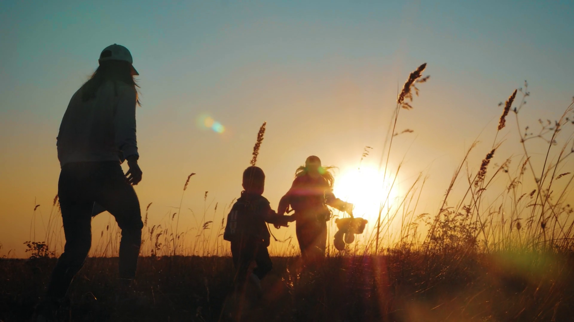 Mother and two children running through the meadow at sunset ...