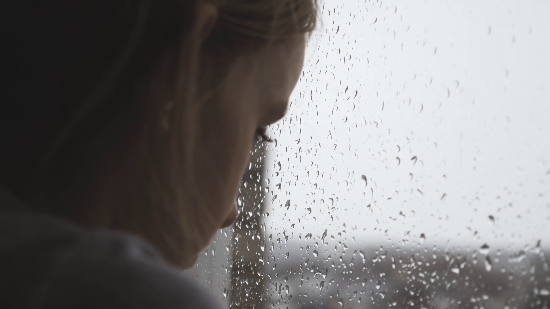 Sad teenager girl looking outside through the window in the rainy day ...