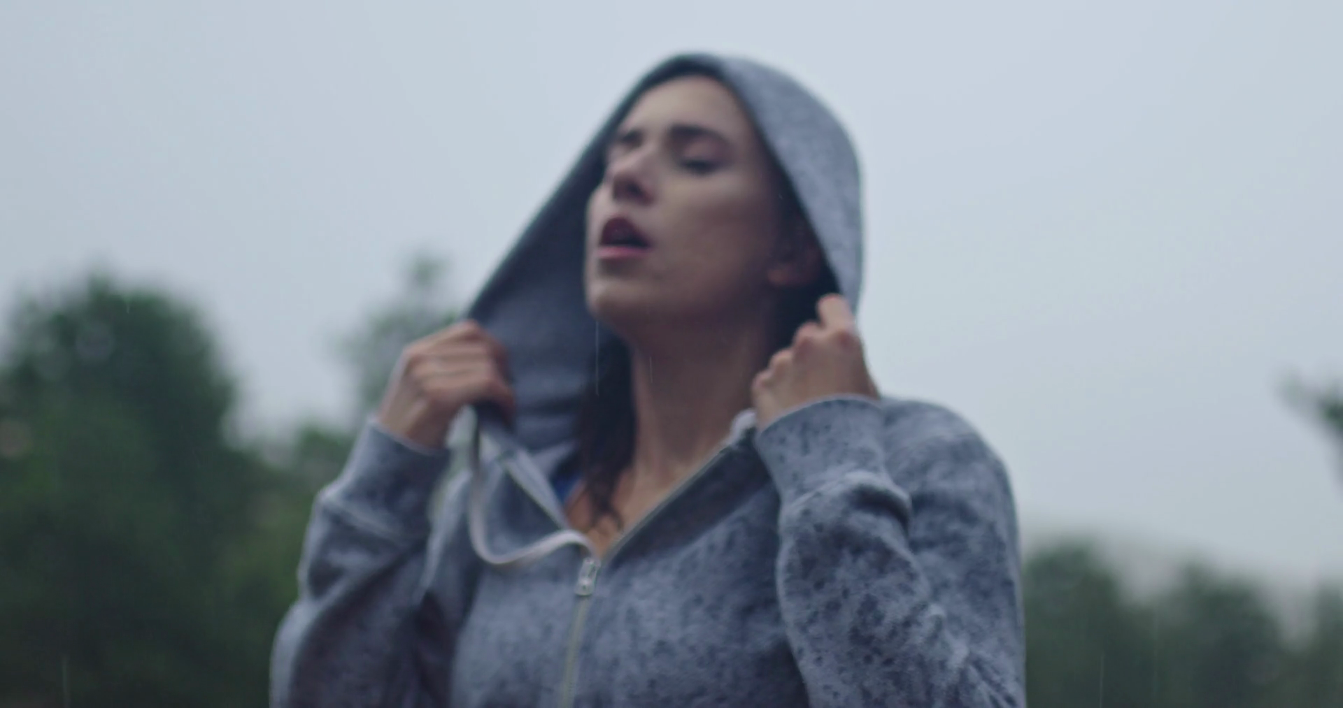 A young woman takes off her hood resting after running on a rainy day ...