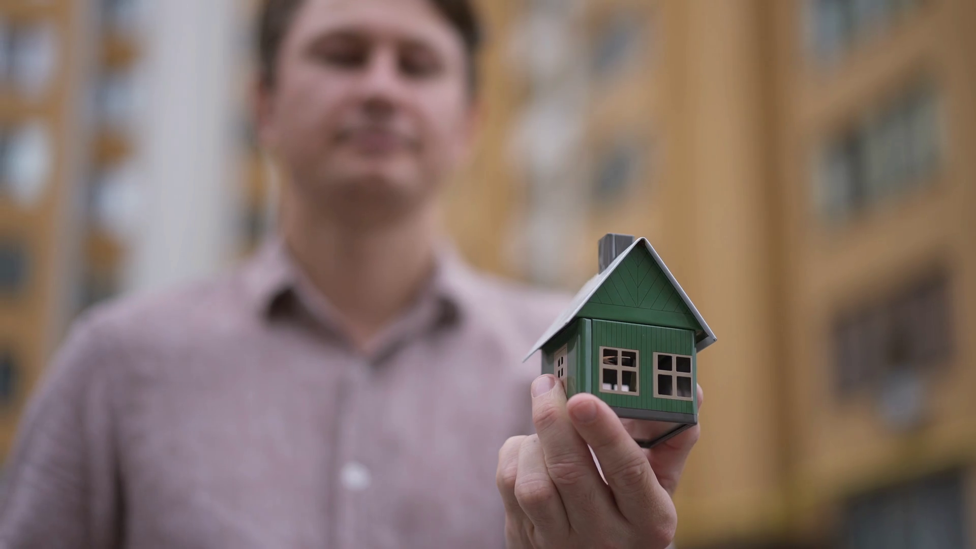 Close-up toy house and key in male hands with blurred happy Caucasian ...