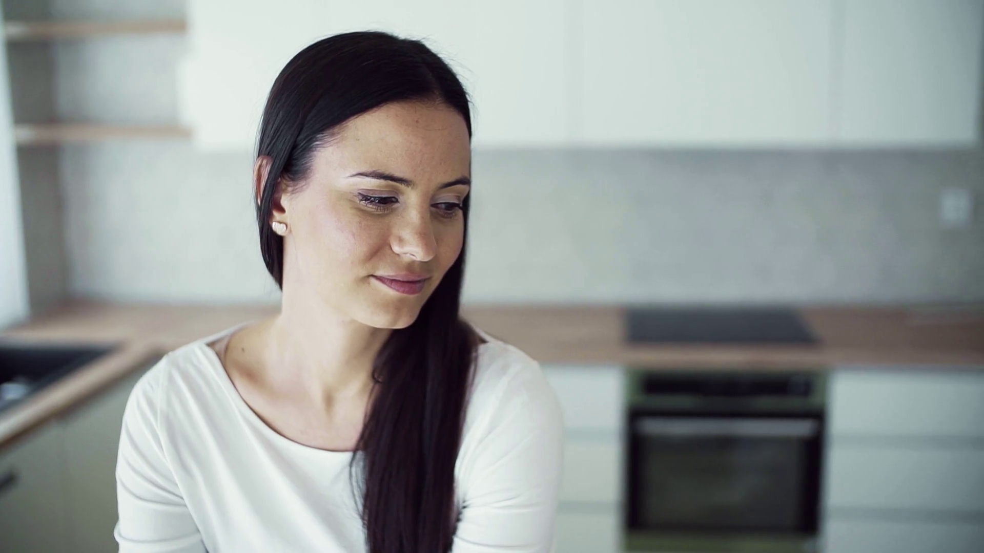 A happy young woman sitting on kitchen counter in new home, resting. A ...
