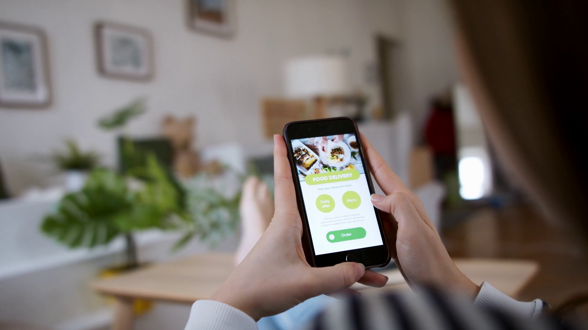 Rear view of young woman with smartphone ordering food at home ...