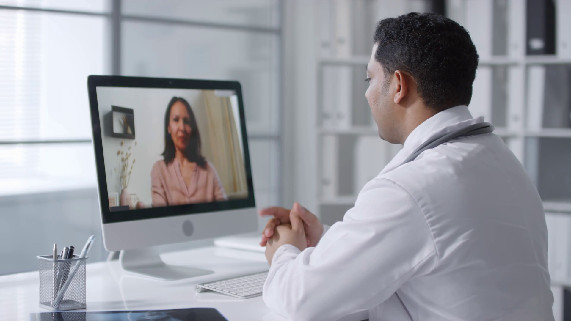 Doctor sitting at desk in front of computer monitor watching his female ...
