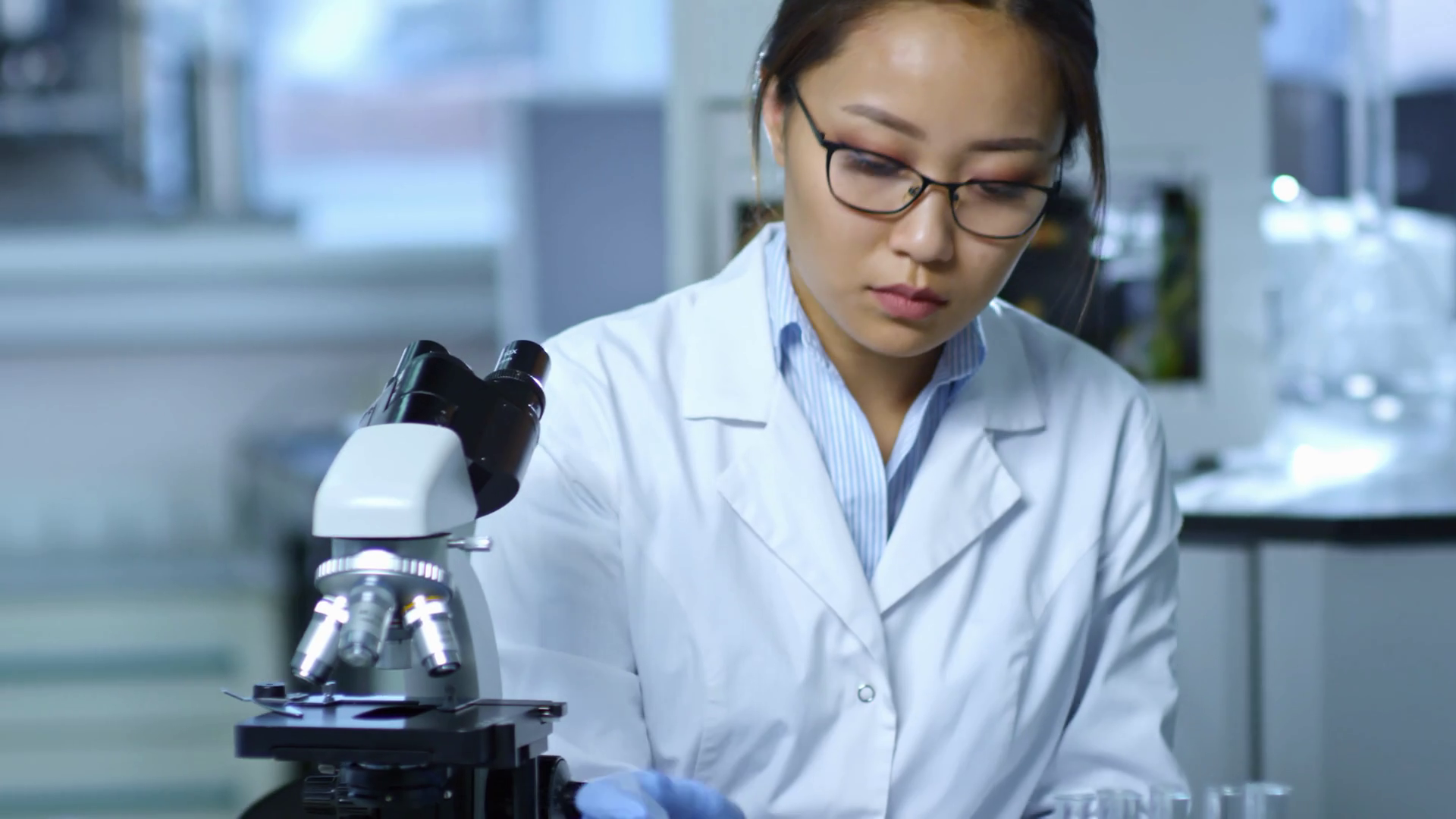 Medium shot of young Asian woman in lab coat, glasses and rubber gloves ...