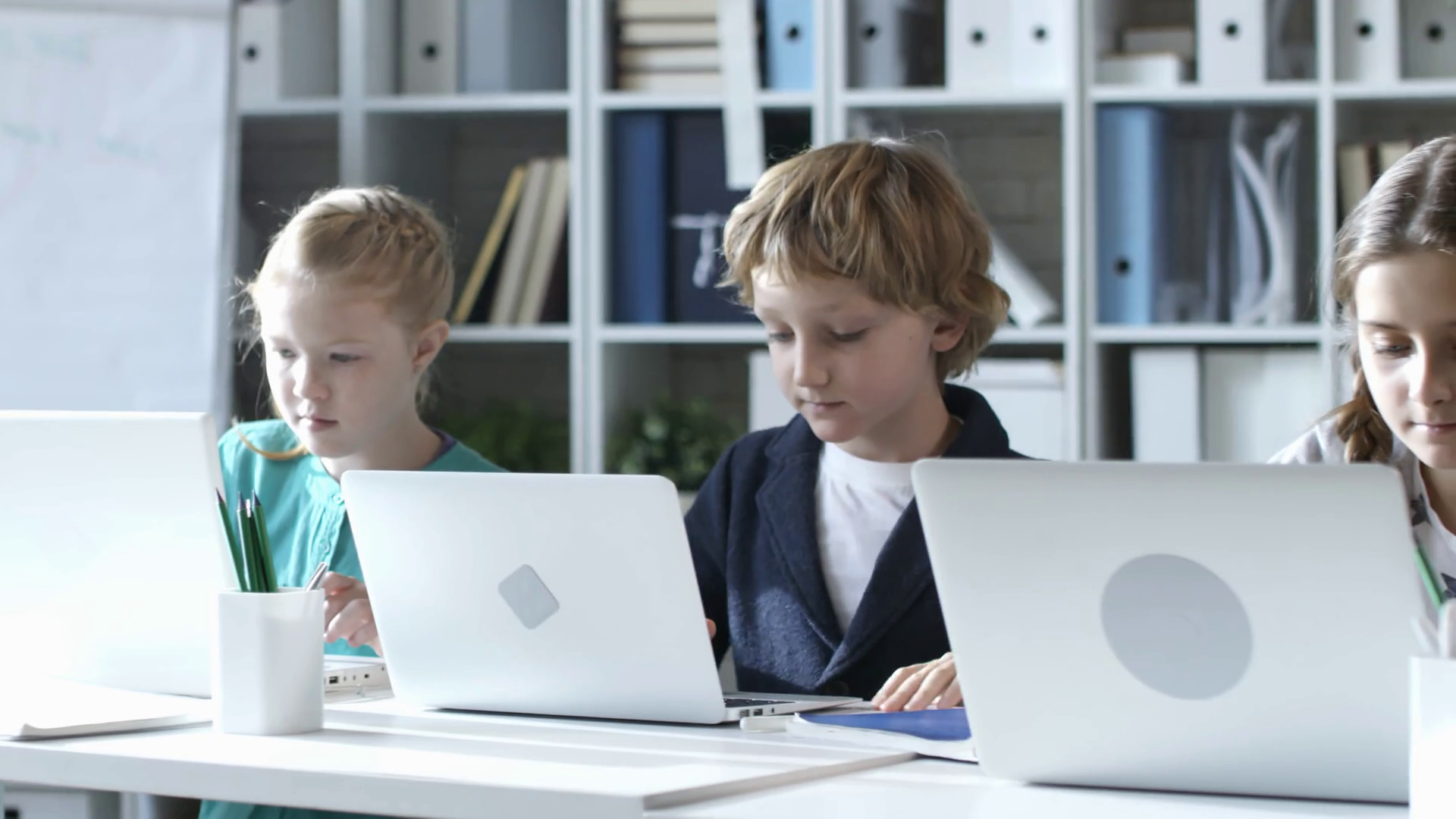 Tracking shot of four primary students working on laptop computers ...