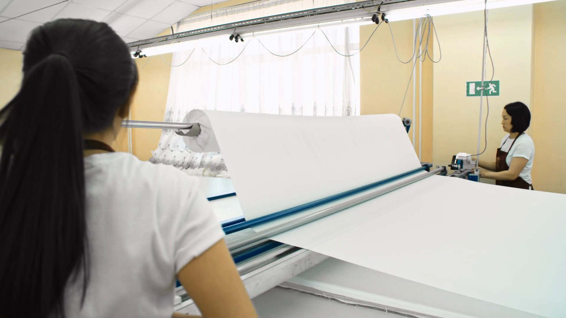 Two Asian women unrolling white fabric and cutting it with automatic ...