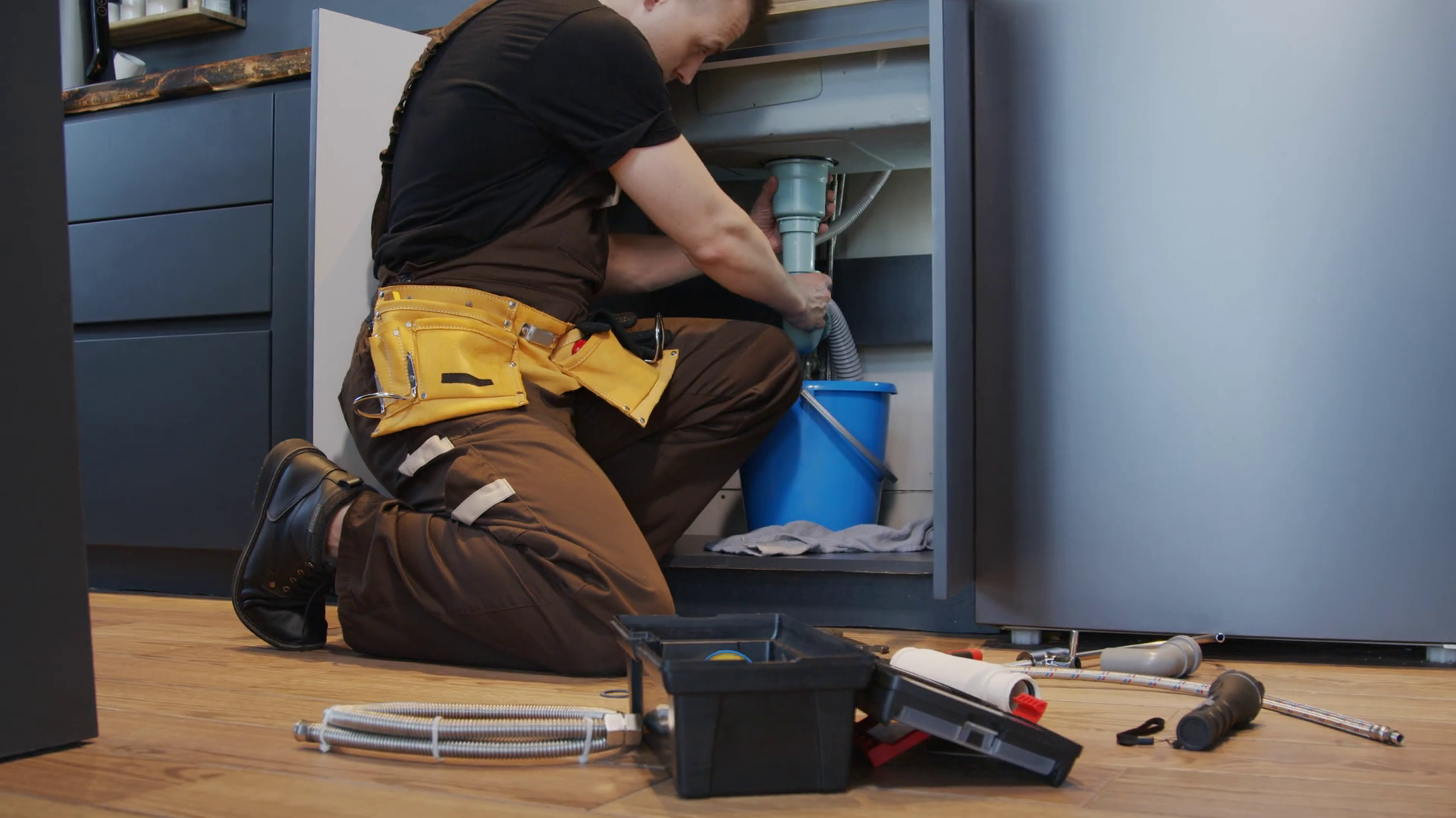Handheld slowmo shot of young male plumber with tool belt kneeling ...