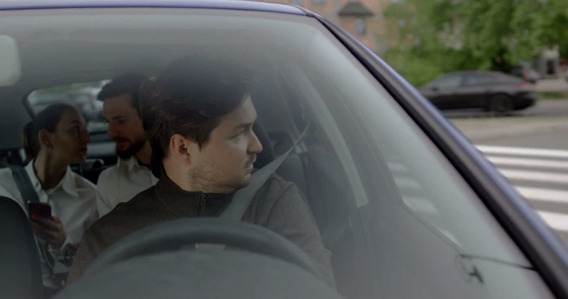 Young uber driver in the car with female and male passenger on backseat ...