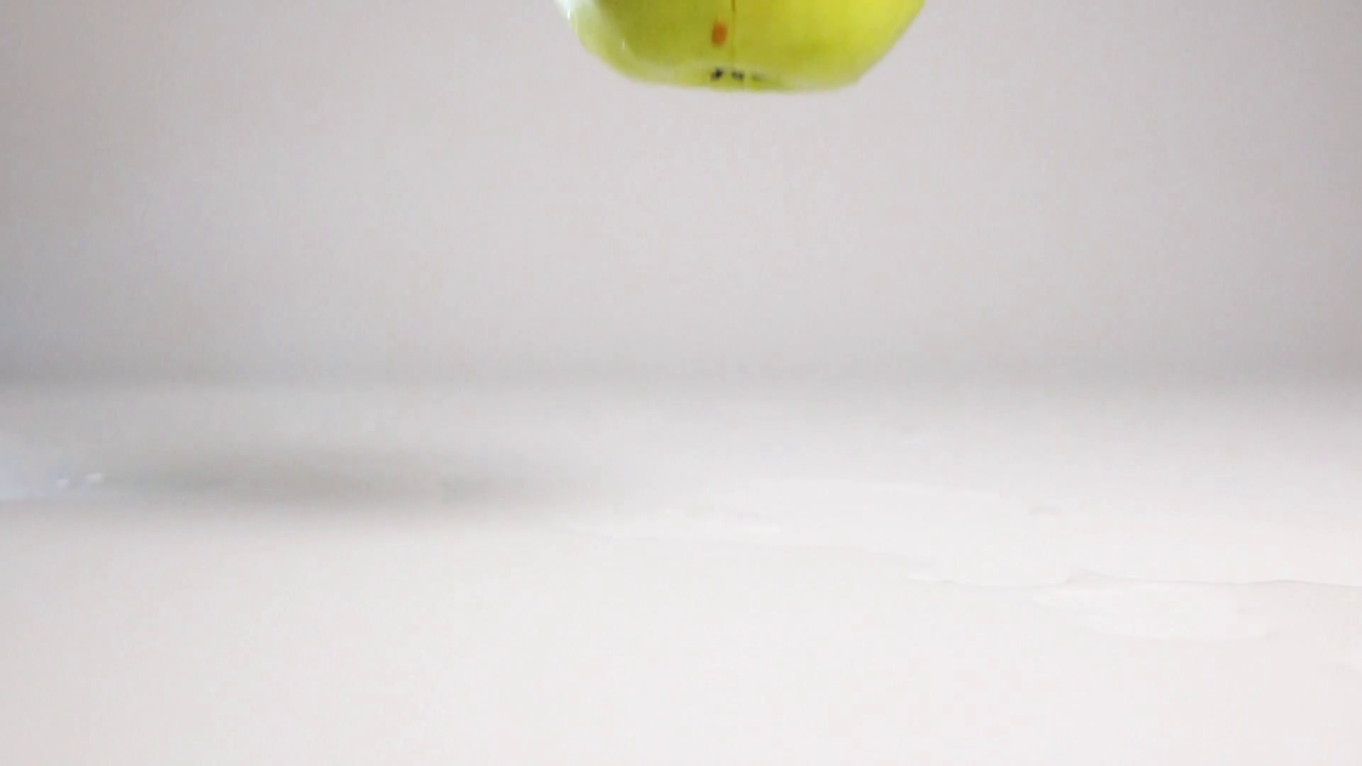 Whole green apple toppling down and breaking on two halfs on wet white ...