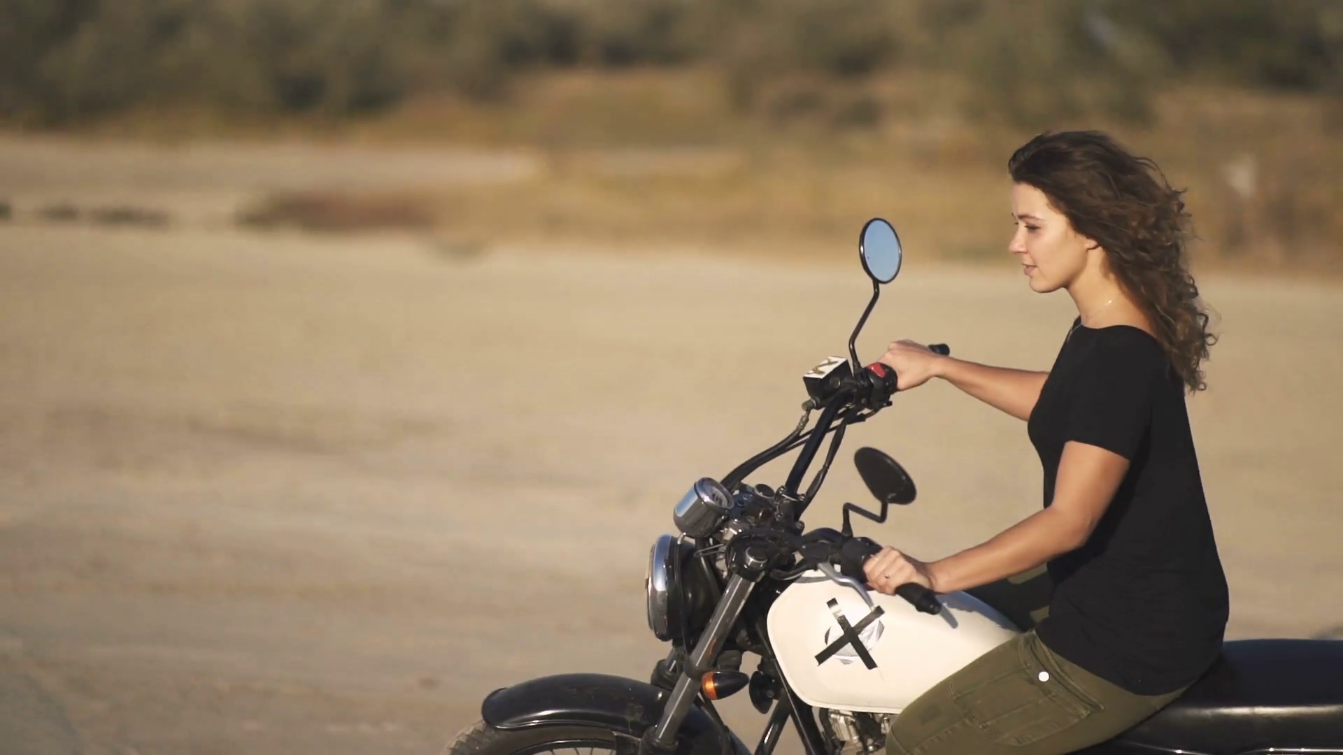 beautiful young woman riding an old cafe racer motorcycle on desert at ...