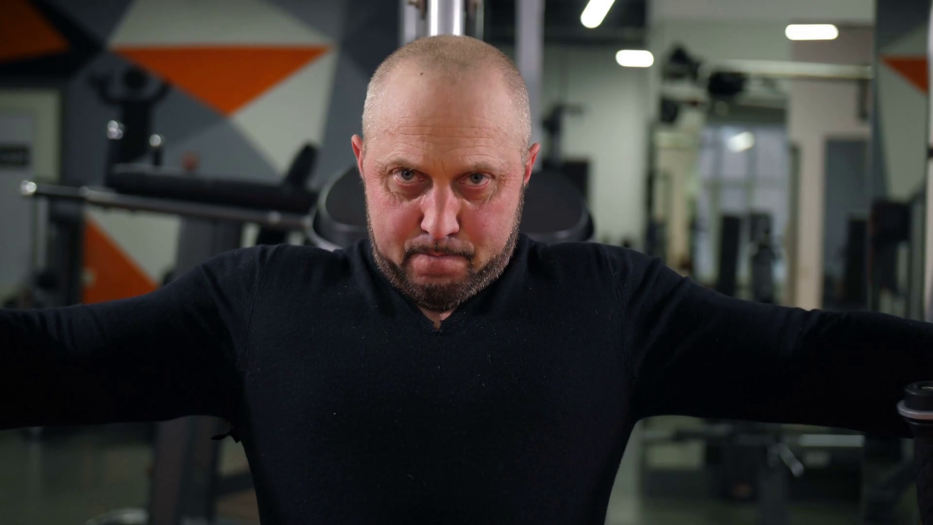 Sportsman in gym is engaged on the simulator. Opens his arms to the ...