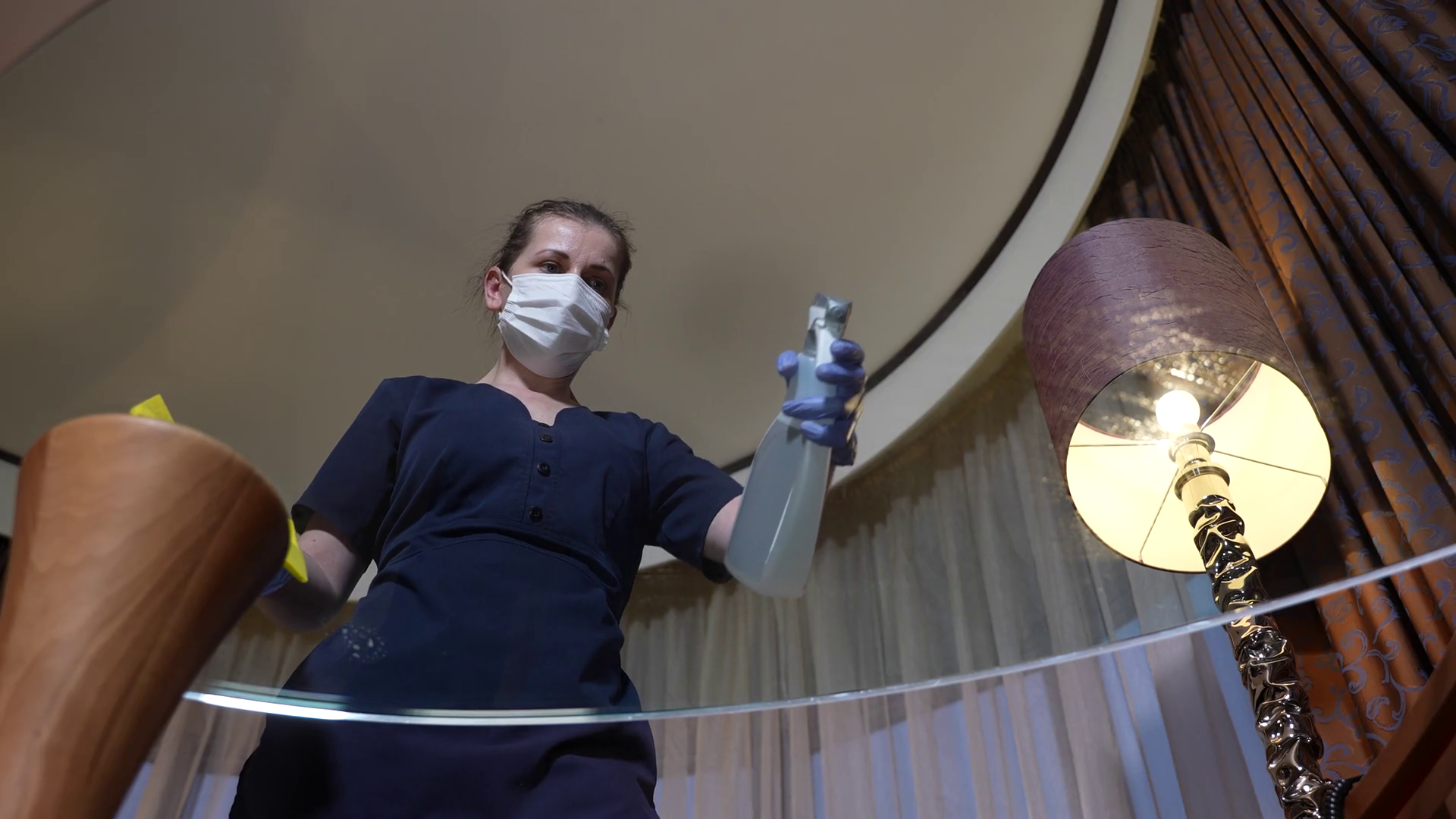 Low angle view of masked maid in gloves spraying disinfectant and ...