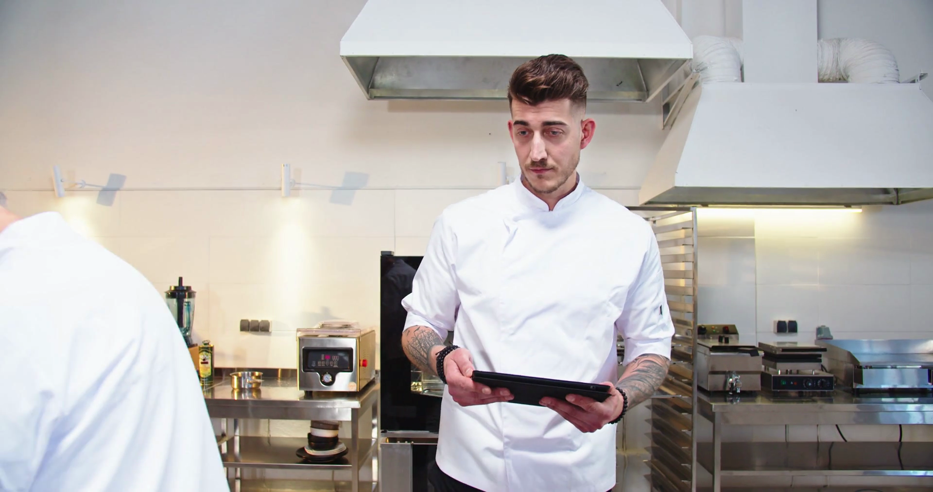 Young Caucasian male chef walking in restaurant kitchen typing on ...