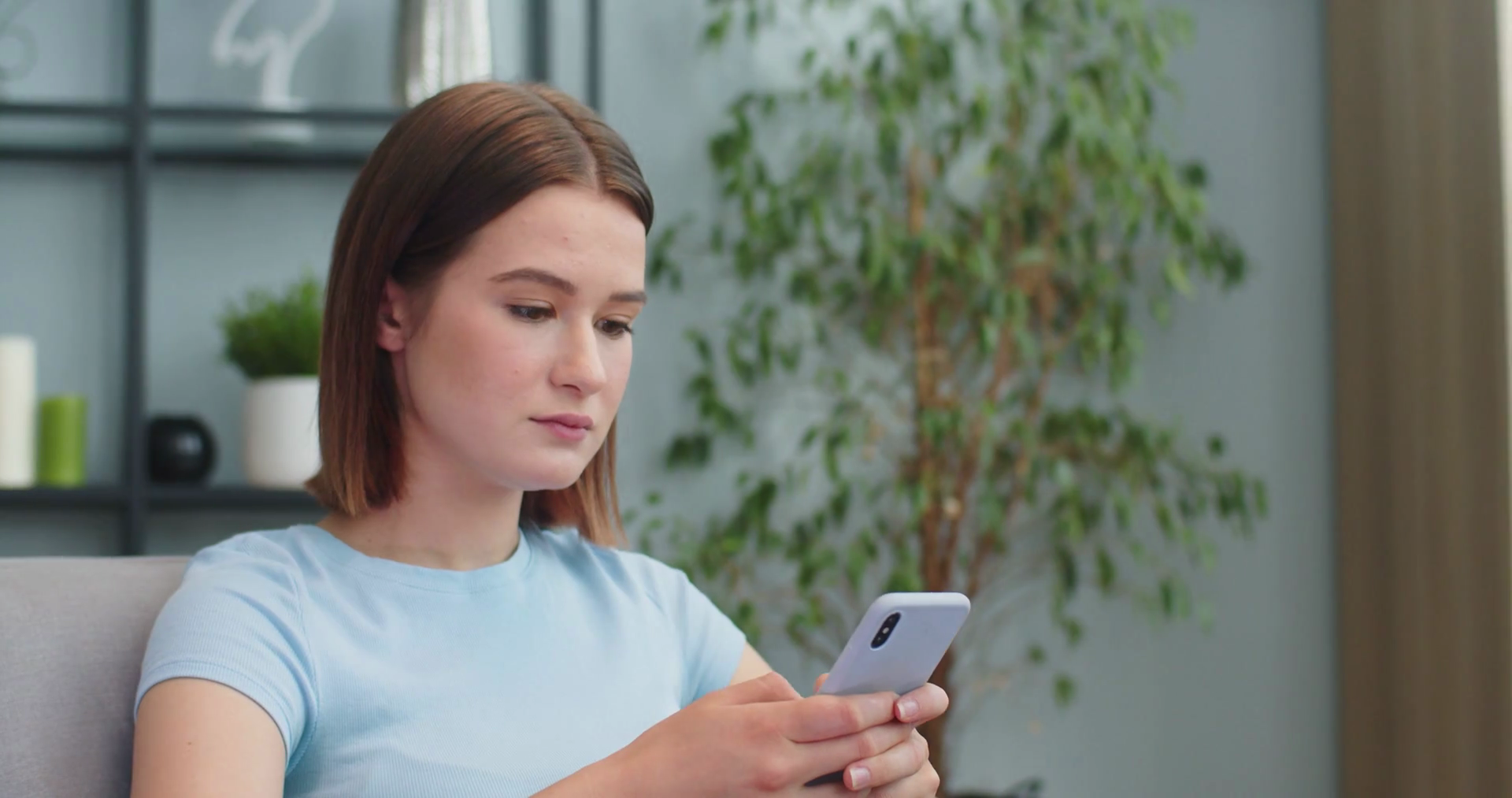 Portrait of Caucasian female sitting on sofa and using smartphone in ...