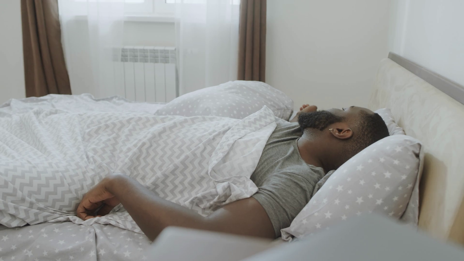 Black man slowly waking up in morning. Young guy taking alarm in hands ...