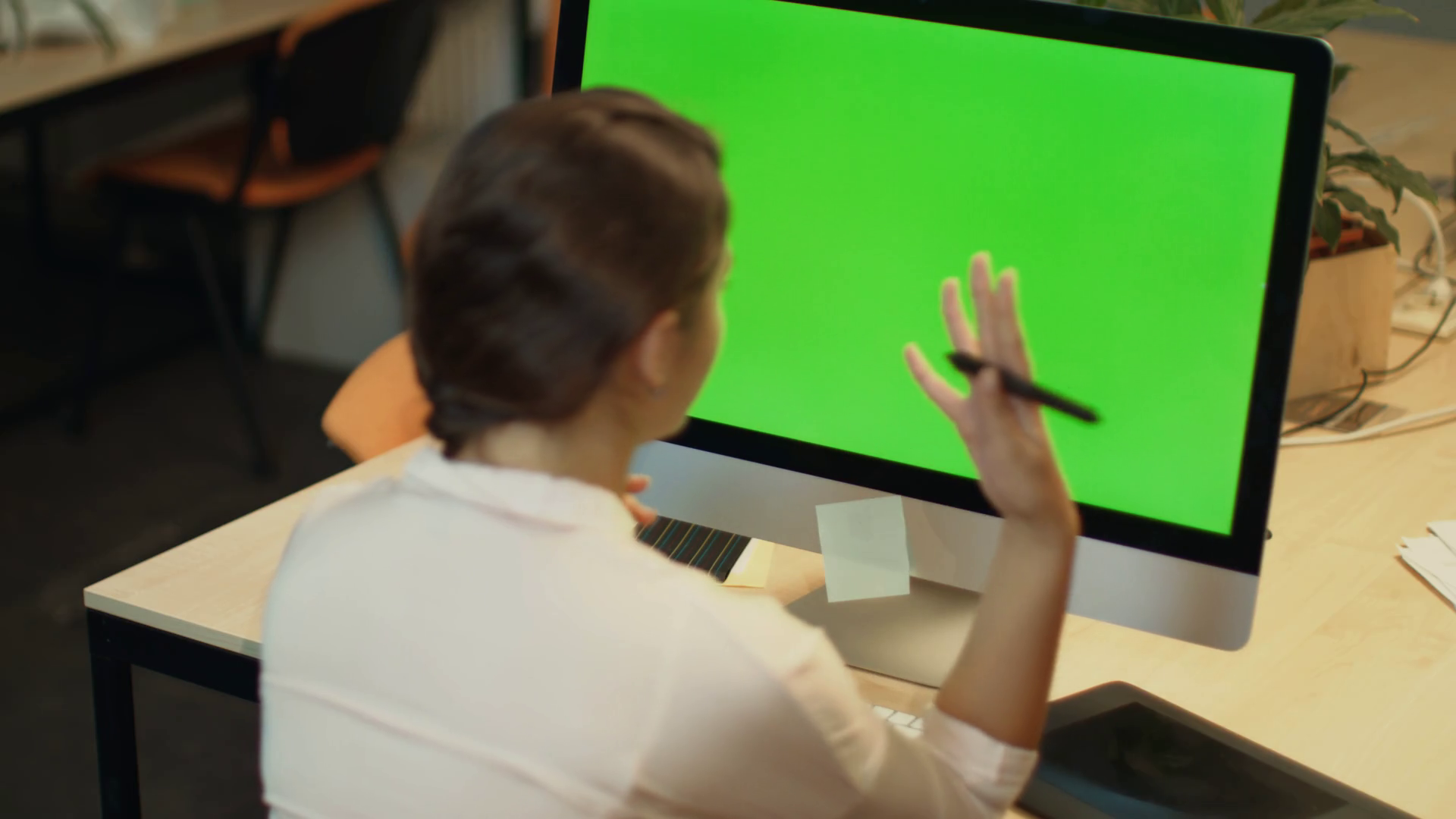 Young woman working on computer with green screen in office. Back view ...