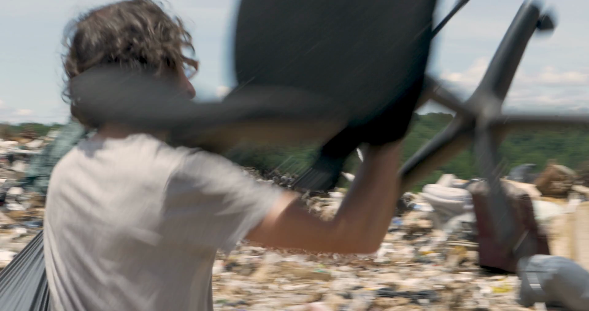 Man throwing a bag of trash and a broken office chair into the landfill ...