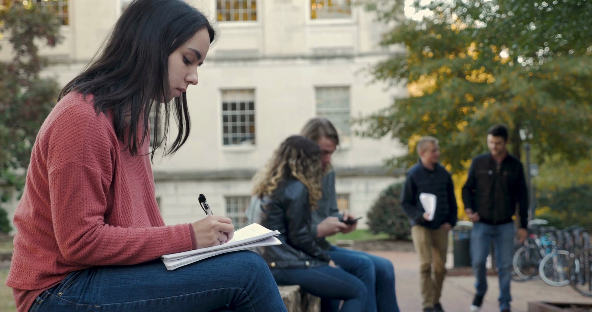 Young woman studying outside writing with a notebook and pen on a ...