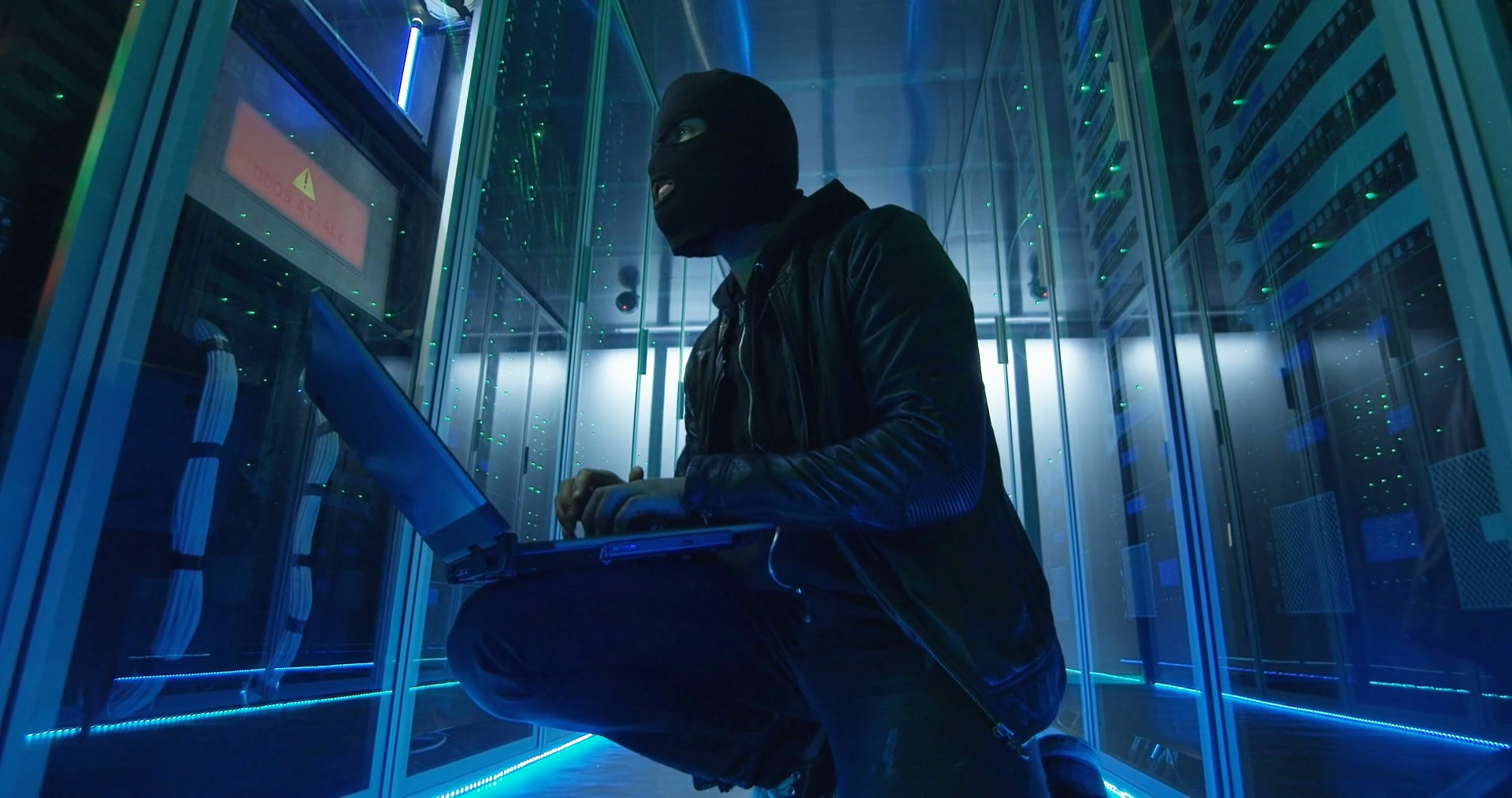 Hacker in black mask using computer and breaking servers of data center ...