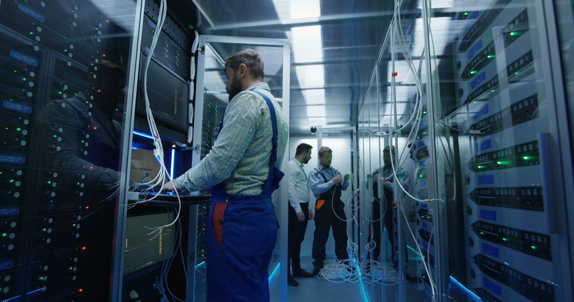Wide shot of a male technicians working in a data center carrying cable ...