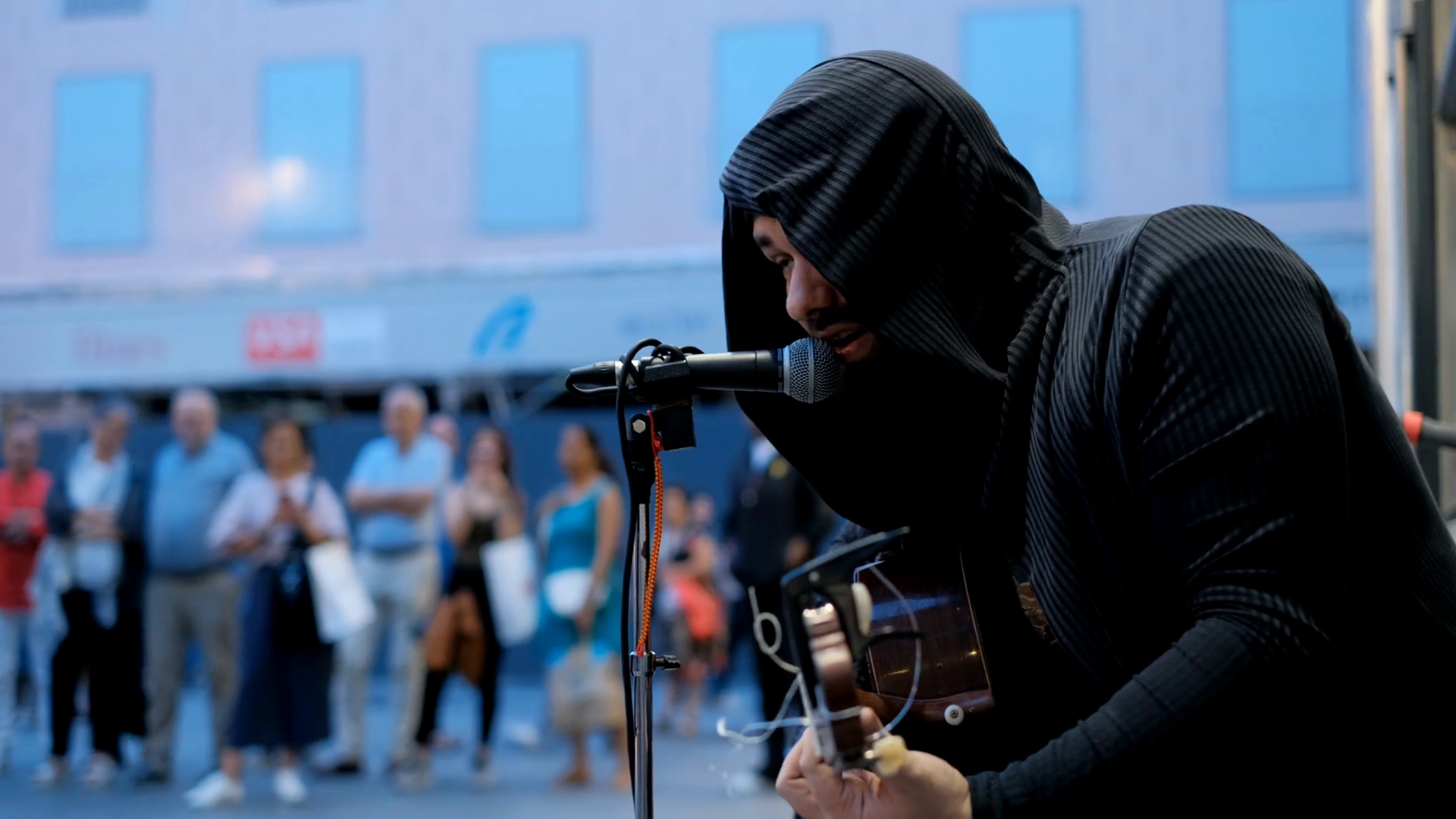 Young man playing guitar and singing song on sidewalk. Street artist ...