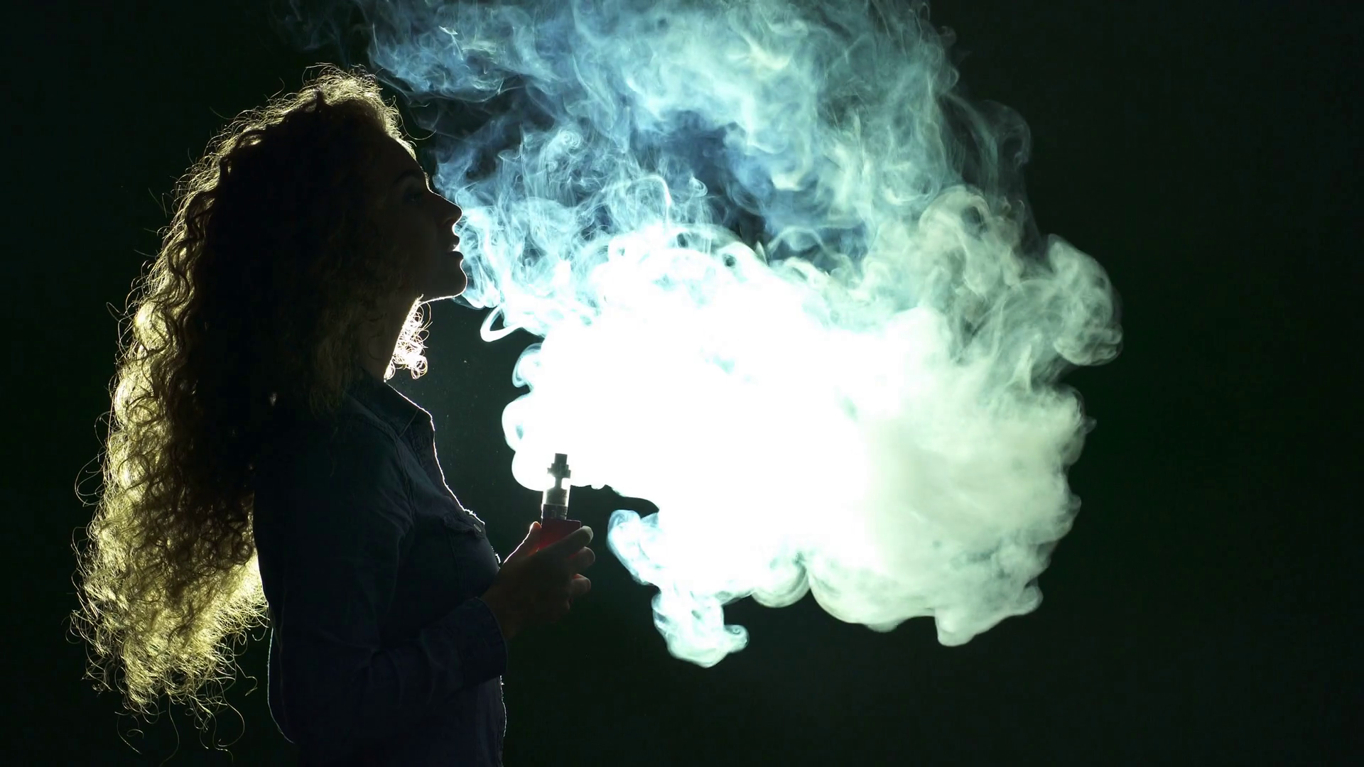 The girl smoke electronic cigarette on the dark background. Real time ...
