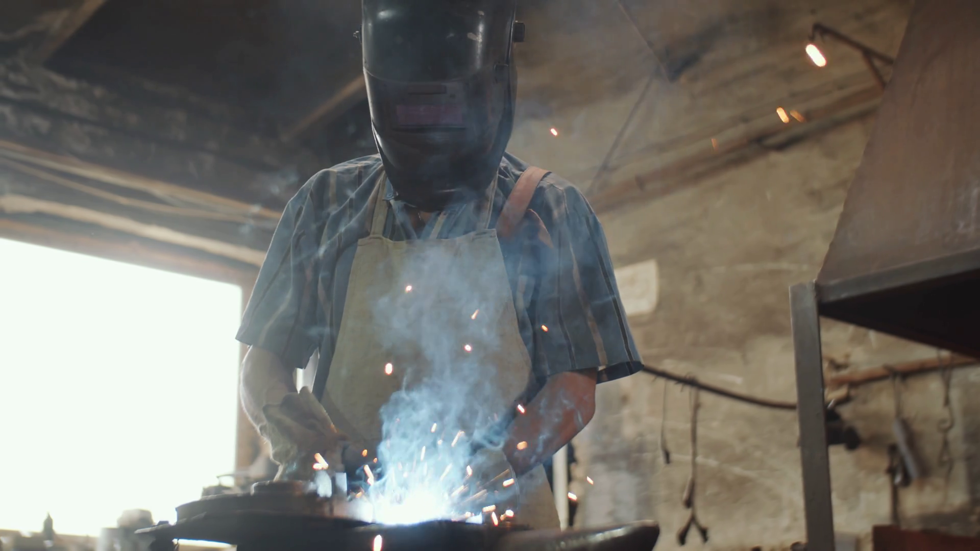 Low angle shot of blacksmith in protective helmet welding iron at work ...