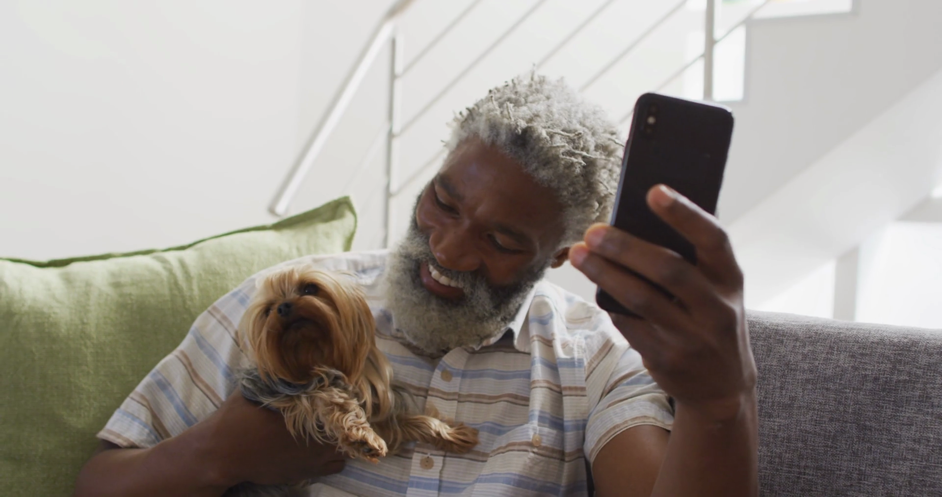 Senior man holding his dog having a video chat on smartphone at home ...