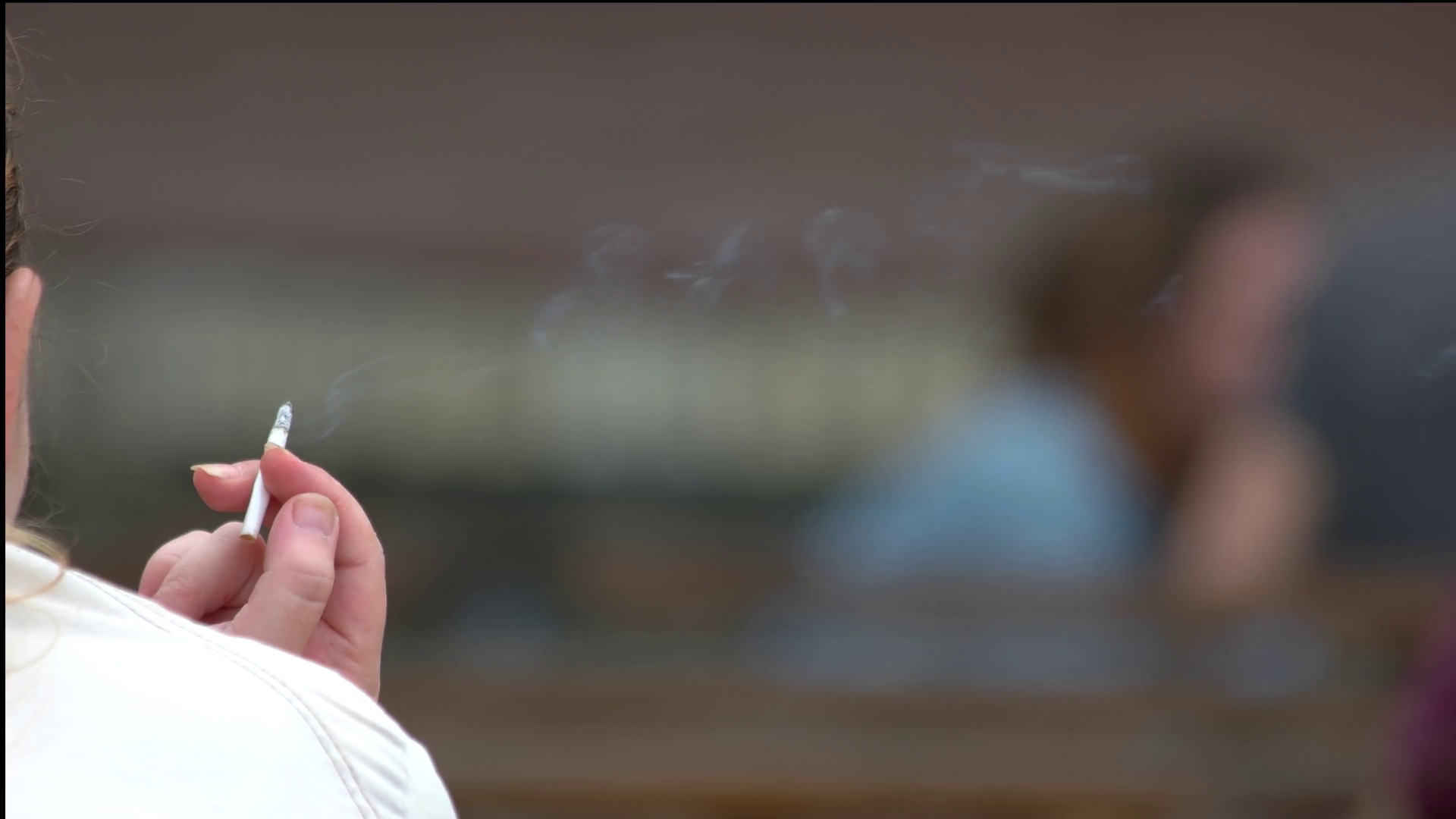 Woman hand holding a cigarette with smoke. Back view, close up ...