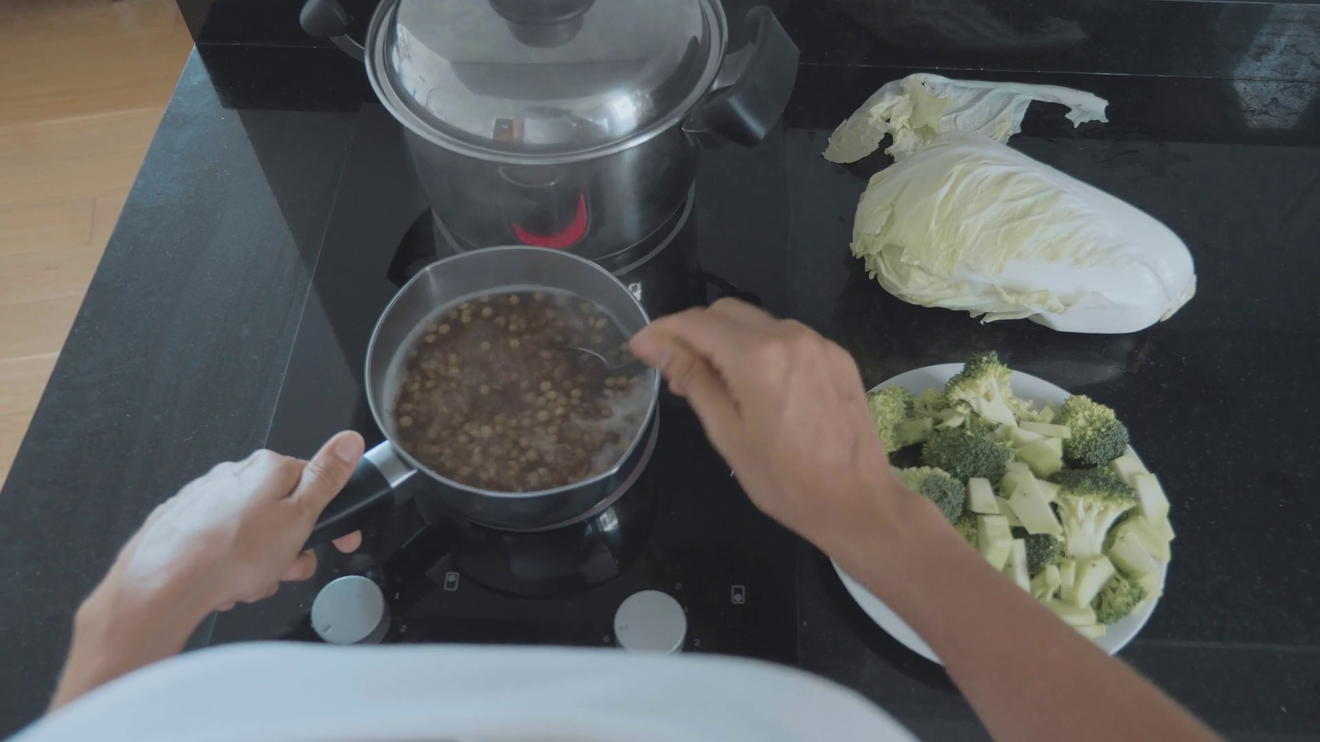 POV of hand with spoon stirring boiling lentils for vegetable soup ...