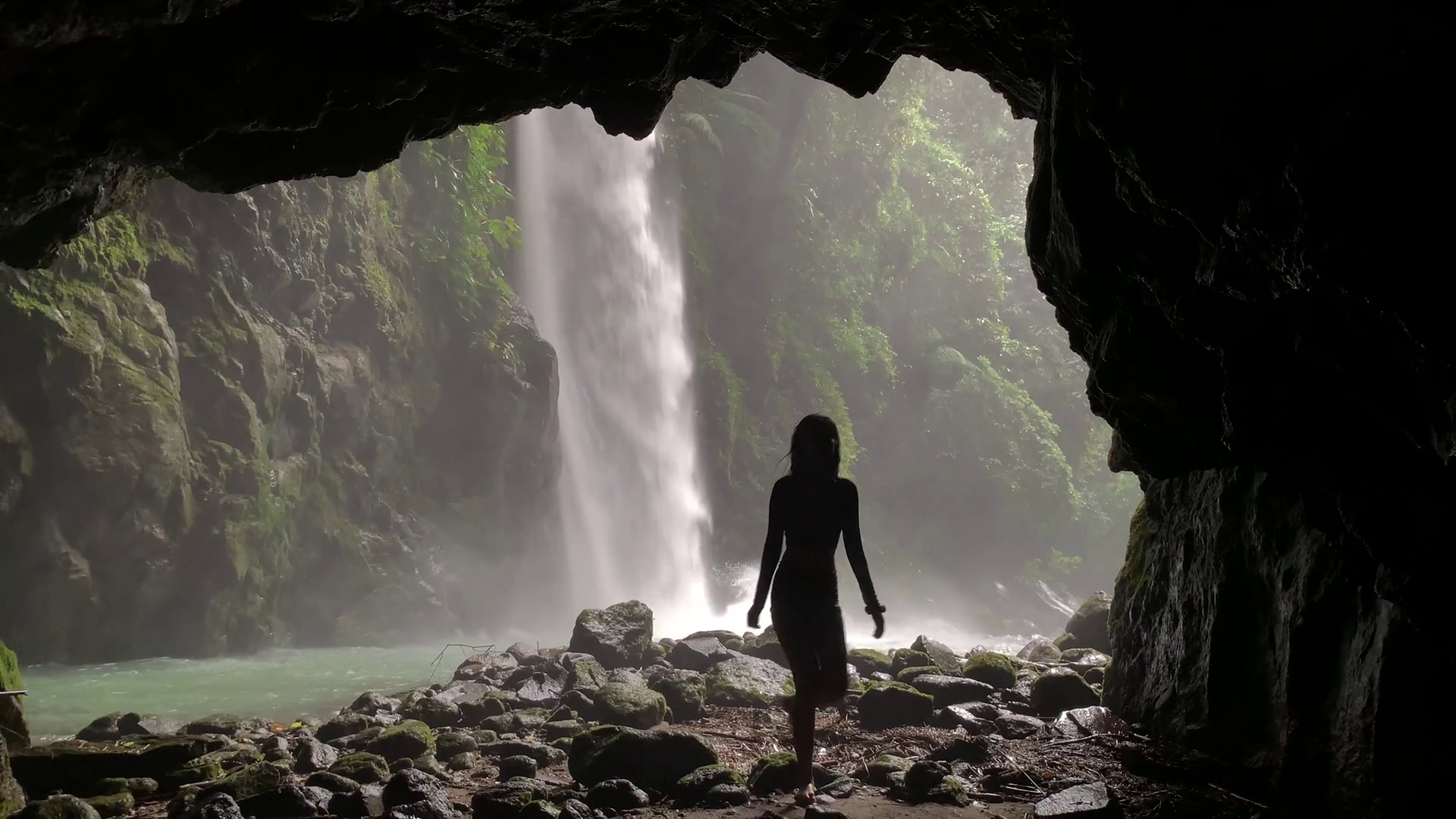 Silhouette of a woman walking inside the cave in a rainforest waterfall ...