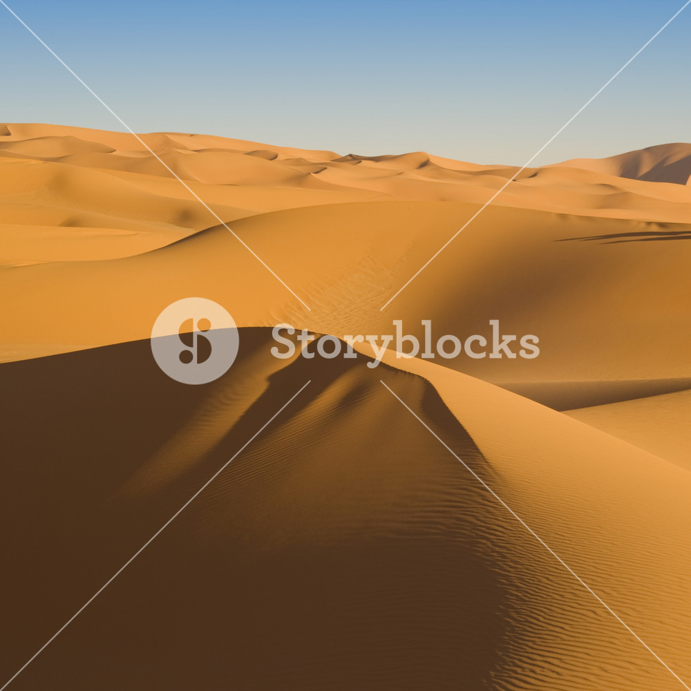 Sunlit sand dunes in the desert under a blue sky Royalty-Free Stock ...