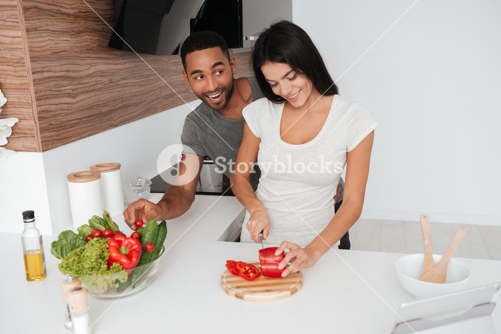 Picture of funny loving couple in the kitchen cooking. Man takes away ...