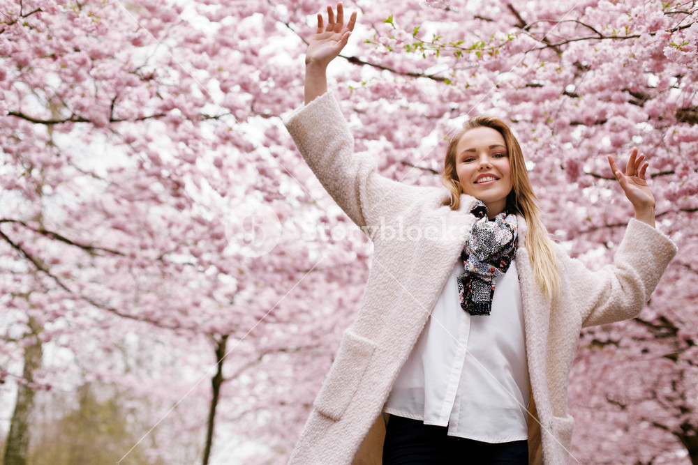Young woman enjoying spring blossom park with arms raised, smiling at ...